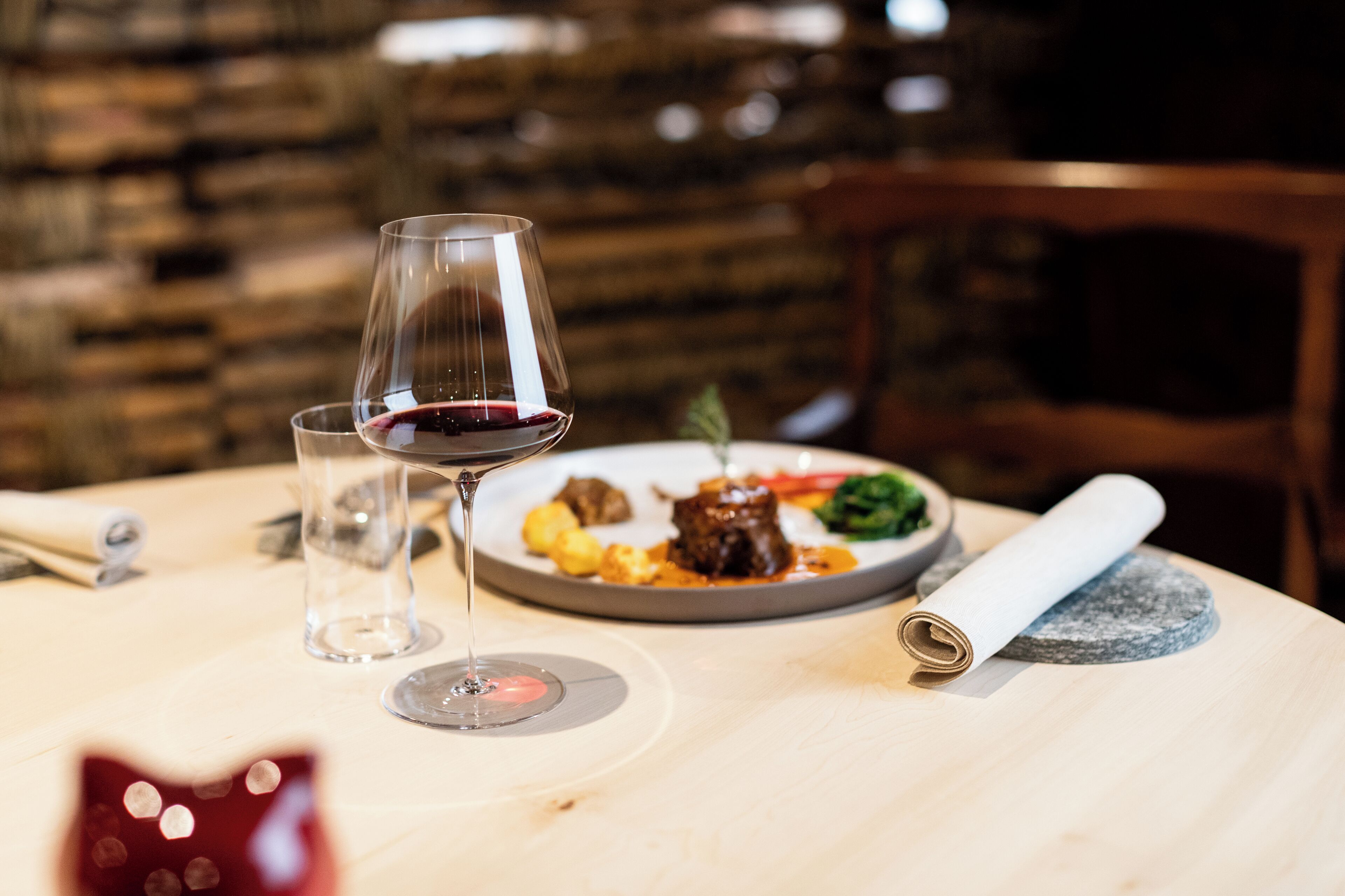 Uma mesa de jantar com um prato de comida, uma taça de vinho e um guardanapo enrolado.