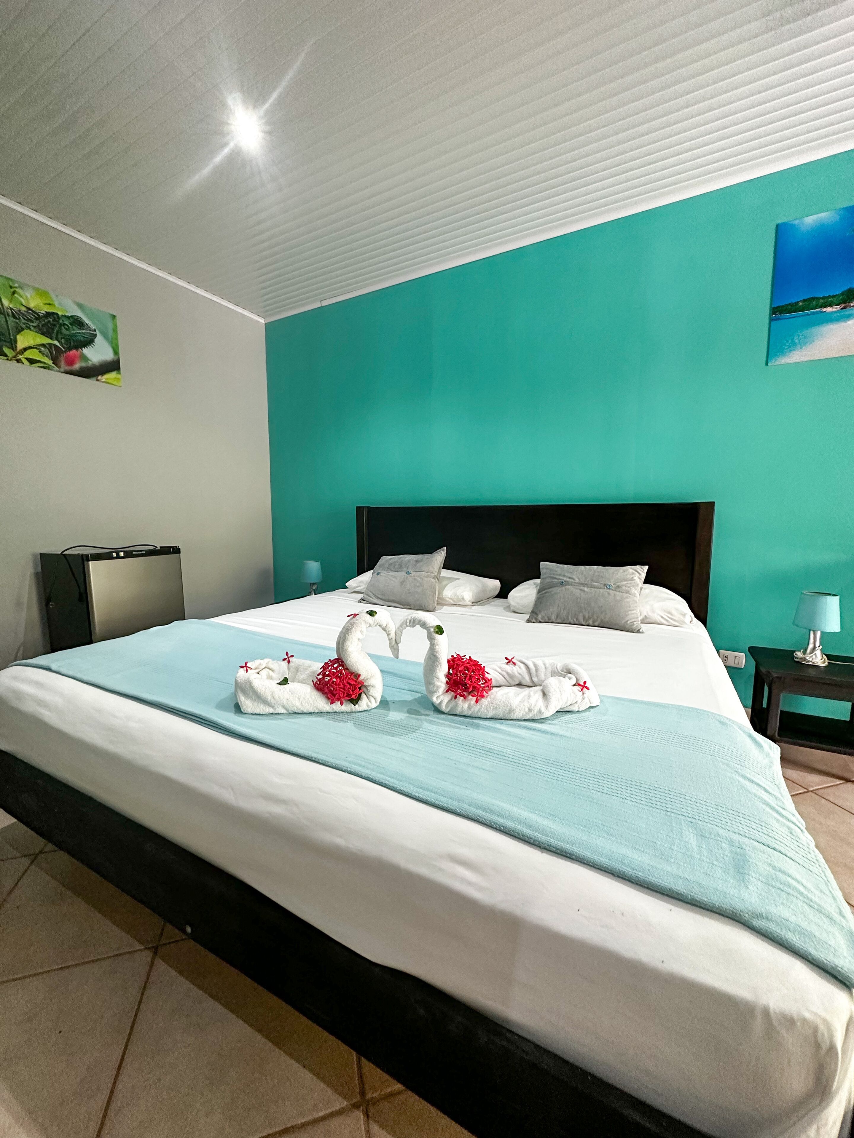Quarto de hotel com cama grande, paredes verde-água e pintura de uma paisagem tropical.