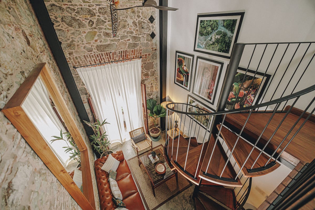 Escadaria em espiral com detalhes em madeira e corrimãos de metal, descendo para um nível inferior.
