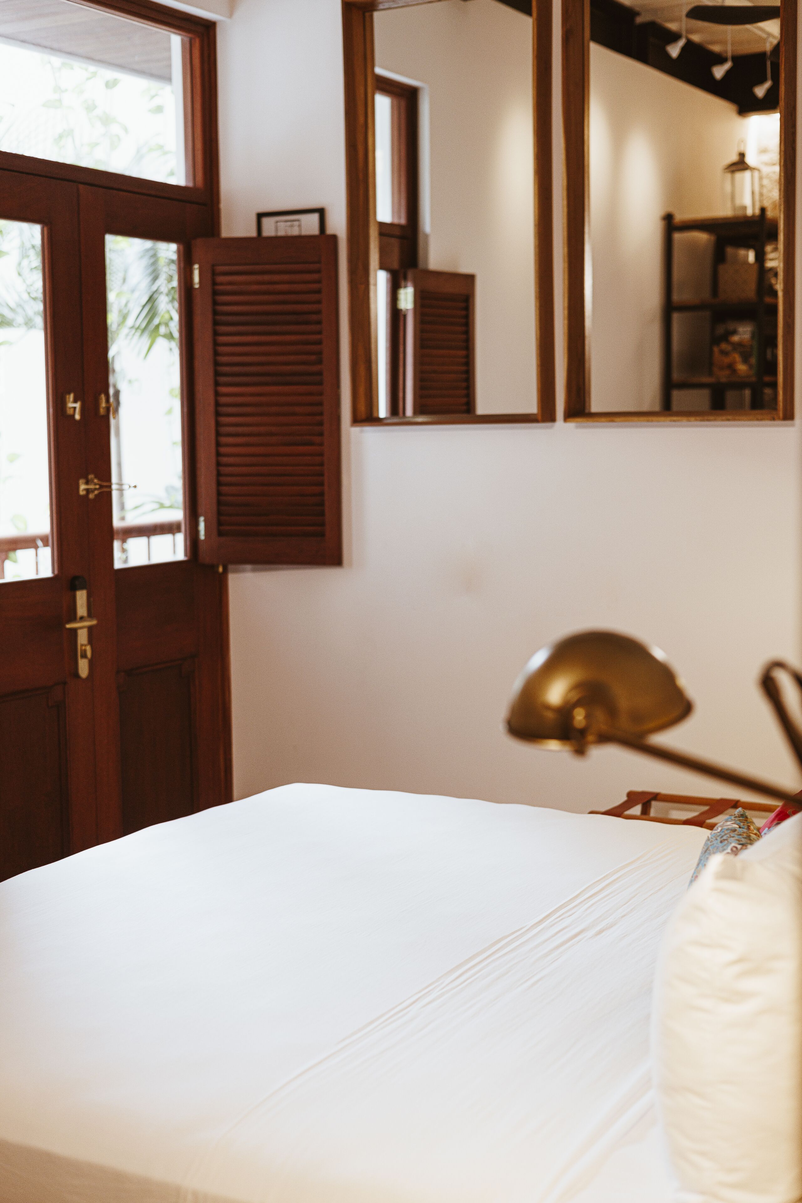 Quarto com cama, porta de madeira com persianas, espelho e abajur.