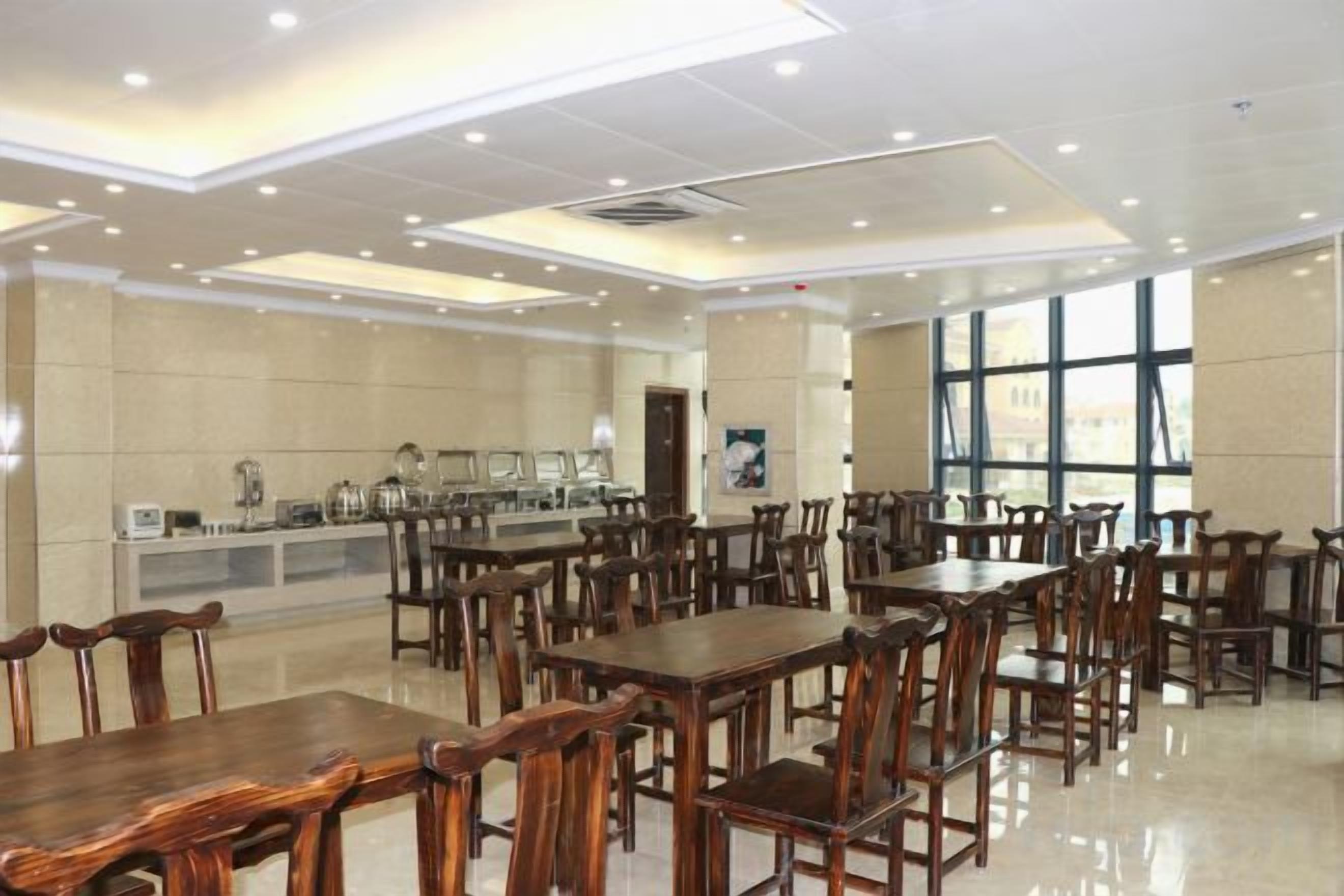 Uma ampla sala de jantar com várias mesas e cadeiras de madeira, um buffet e grandes janelas que proporcionam iluminação natural.