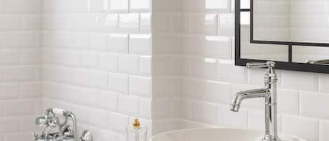 Casa de banho com azulejos brancos estilo metrô, uma pia branca, um porta-toalhas preto e branco, e um espelho com moldura preta.