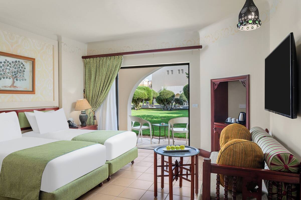 Quarto de hotel com duas camas, uma mesa de jantar, um sofá e uma televisão.