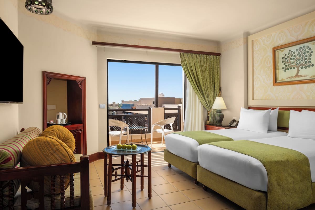 Quarto de hotel com duas camas, varanda, área de refeições e televisão.