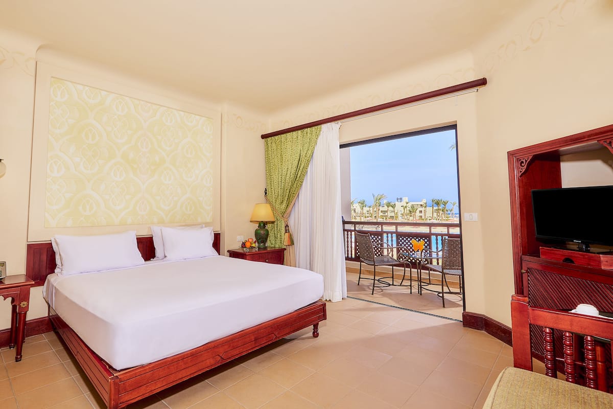 Quarto de hotel com cama grande, televisão, varanda com cadeiras e parede com padrão.