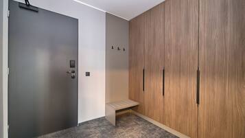 Quarto com porta cinza, um banco e guarda-roupa de madeira com puxadores pretos.