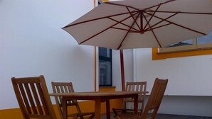 Uma mesa de madeira e quatro cadeiras sob um guarda-sol grande.