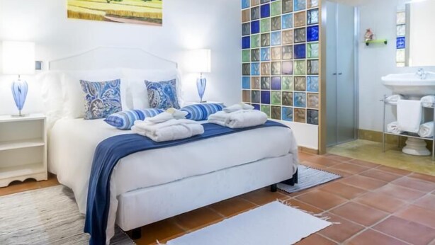 Quarto com cama, mesas de cabeceira, um armário de noite, uma janela ampla com vista e um banheiro com pia e espelho.