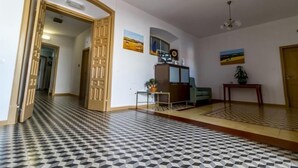 Um corredor com piso estampado, uma porta de madeira, uma pequena mesa com uma planta e um espelho fixado na parede.