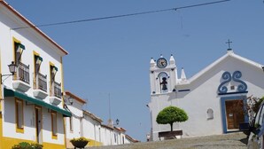 Uma rua de paralelepípedos com edifícios, uma igreja com torre do relógio e um banco.