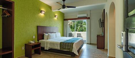 Quarto de hotel com uma cama, mesa de cabeceira, ventilador de teto e vista para o exterior.
