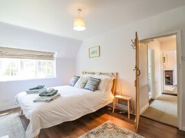 Quarto com cama, mesa de cabeceira, abajur, janela com cortinas, porta e vista para uma lareira.