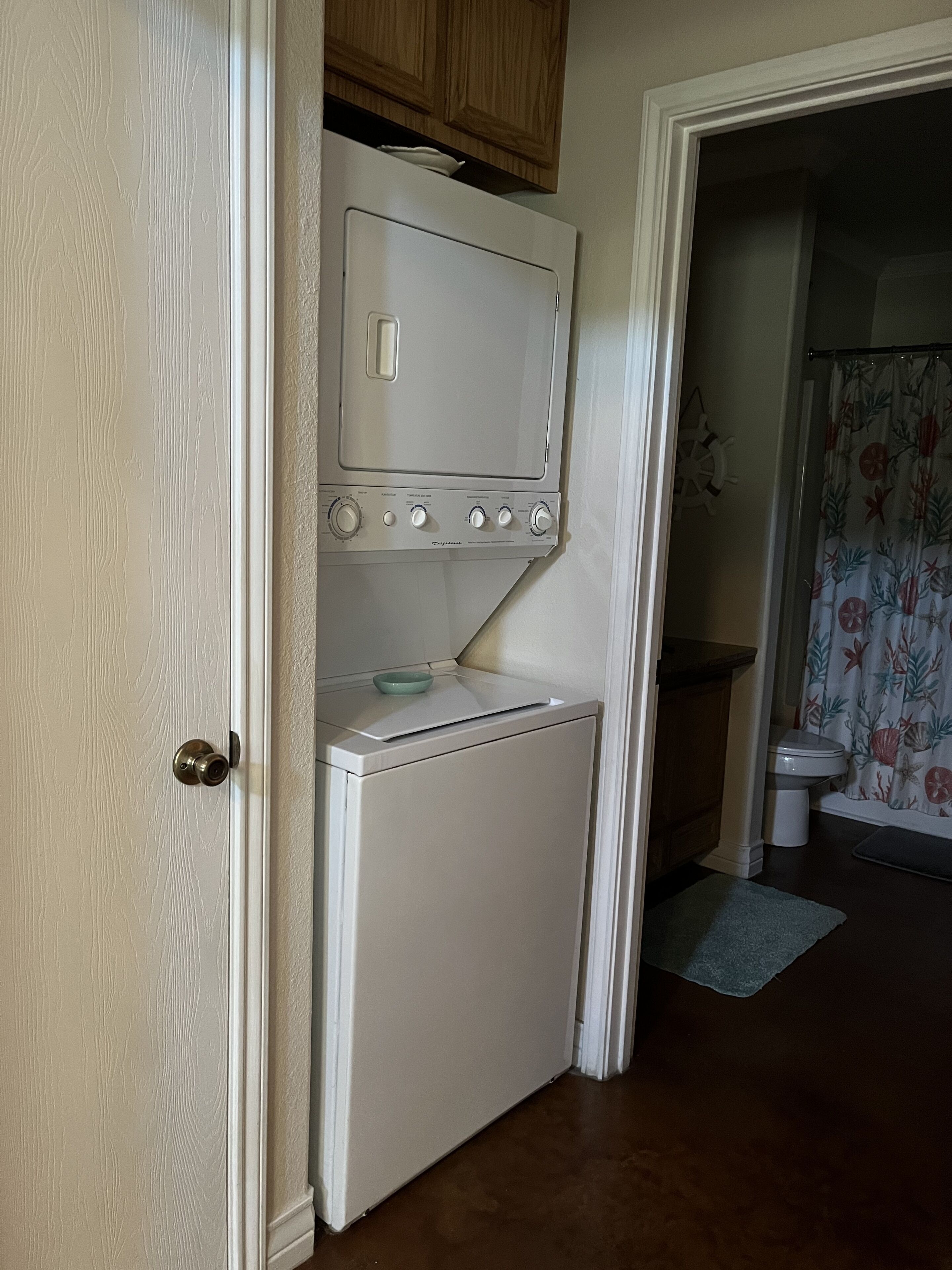 Uma cozinha compacta com geladeira e forno embutidos, um armário de madeira acima e um banheiro com vaso sanitário e cortina de chuveiro.