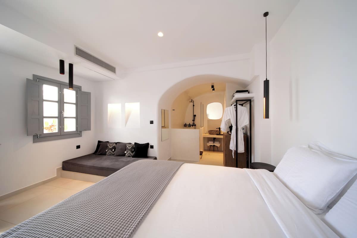 Quarto moderno com uma cama grande, área de estar, guarda-roupa e casa de banho visível através de um arco.