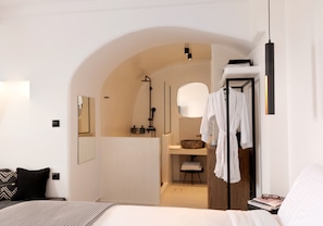 Quarto de hotel moderno com uma cama, mesa de cabeceira, espelho, toucador com pia e closet espaçoso.