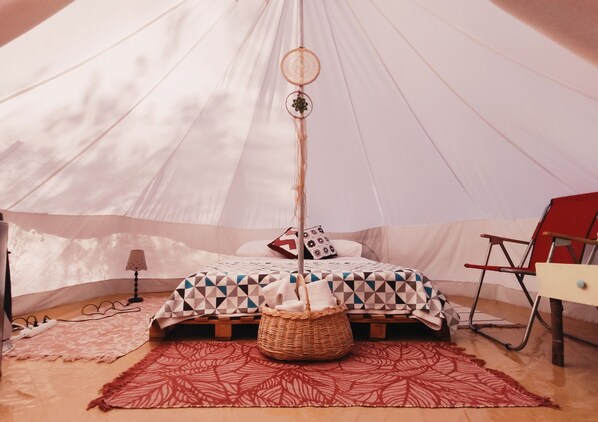 Uma tenda com uma cama, um tapete vermelho estampado, uma cesta de vime, um abajur e uma cadeira vermelha.