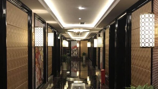 Um corredor com piso espelhado, luminárias na parede e um lustre central.
