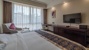 Quarto de hotel com uma cama grande, uma escrivaninha com televisão de tela plana, uma cadeira e uma pequena mesa.