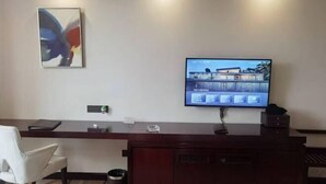 Uma área de recepção de hotel, com balcão, cadeira, televisão na parede e uma obra de arte emoldurada sobre o balcão.