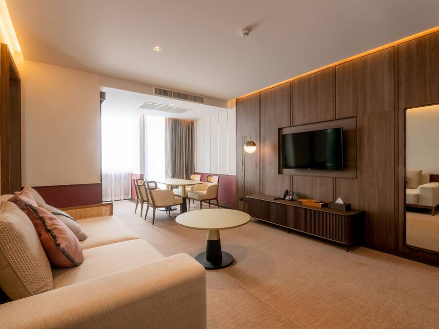 Quarto de hotel moderno com sofá, mesa de jantar, televisão e um espelho grande.