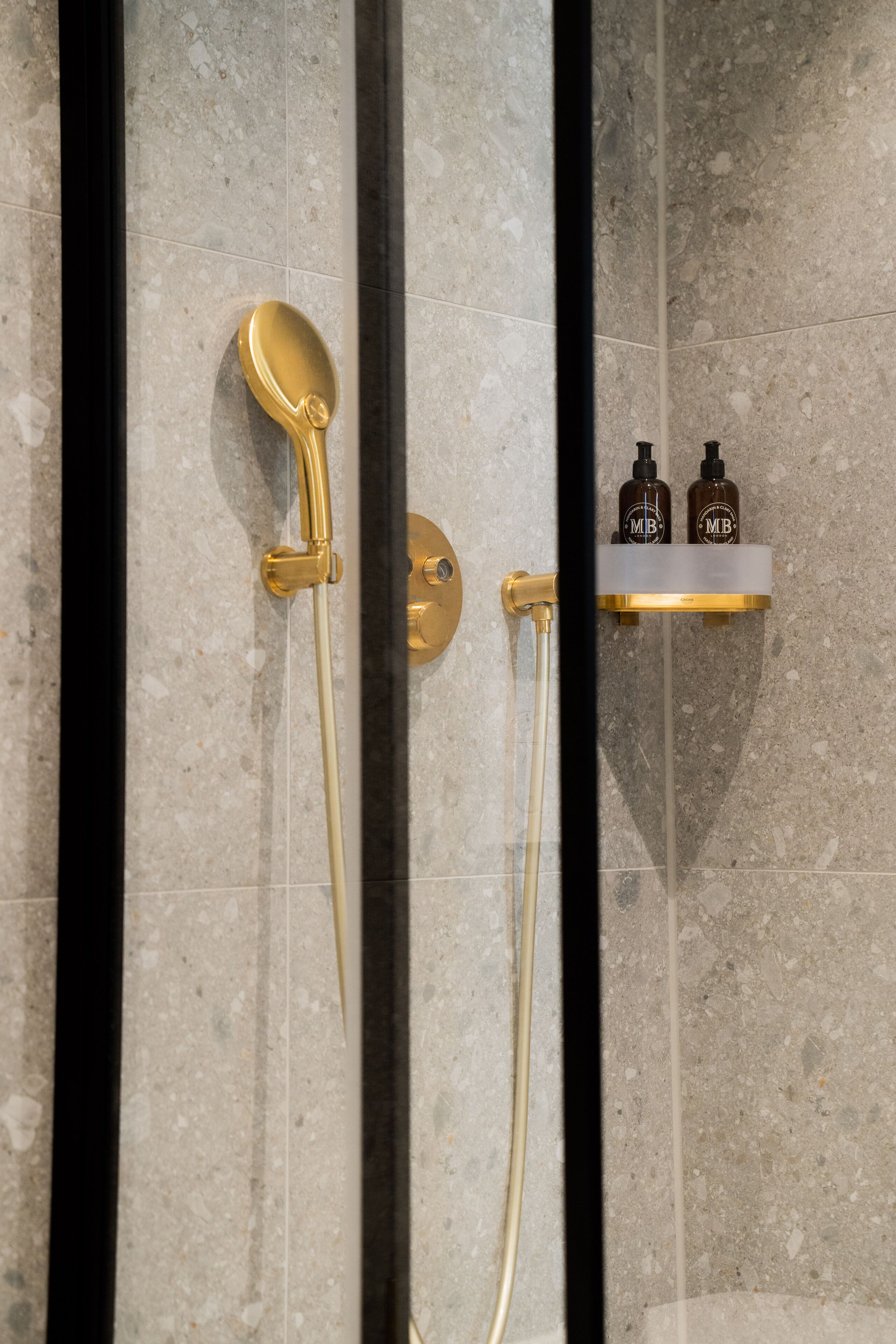 Chuveiro dourado com dois frascos de shampoo em uma prateleira.