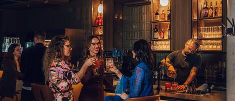 Uma área de bar com clientes sentados e um bartender preparando bebidas.