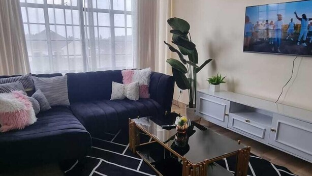 Uma sala de estar com um sofá escuro, uma mesa de centro e uma janela grande com cortinas.