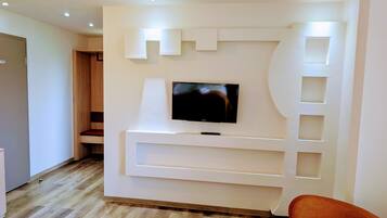 Uma sala de estar moderna com uma TV de tela plana presa a uma parede branca, piso de madeira e uma poltrona vermelha.