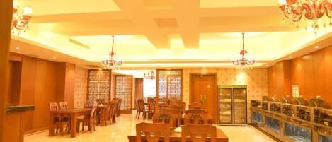 Espaço de refeições de hotel com várias mesas e cadeiras, um candelabro e um balcão de recepção.