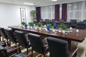 Uma sala de conferências com uma mesa comprida, cadeiras pretas e uma planta.
