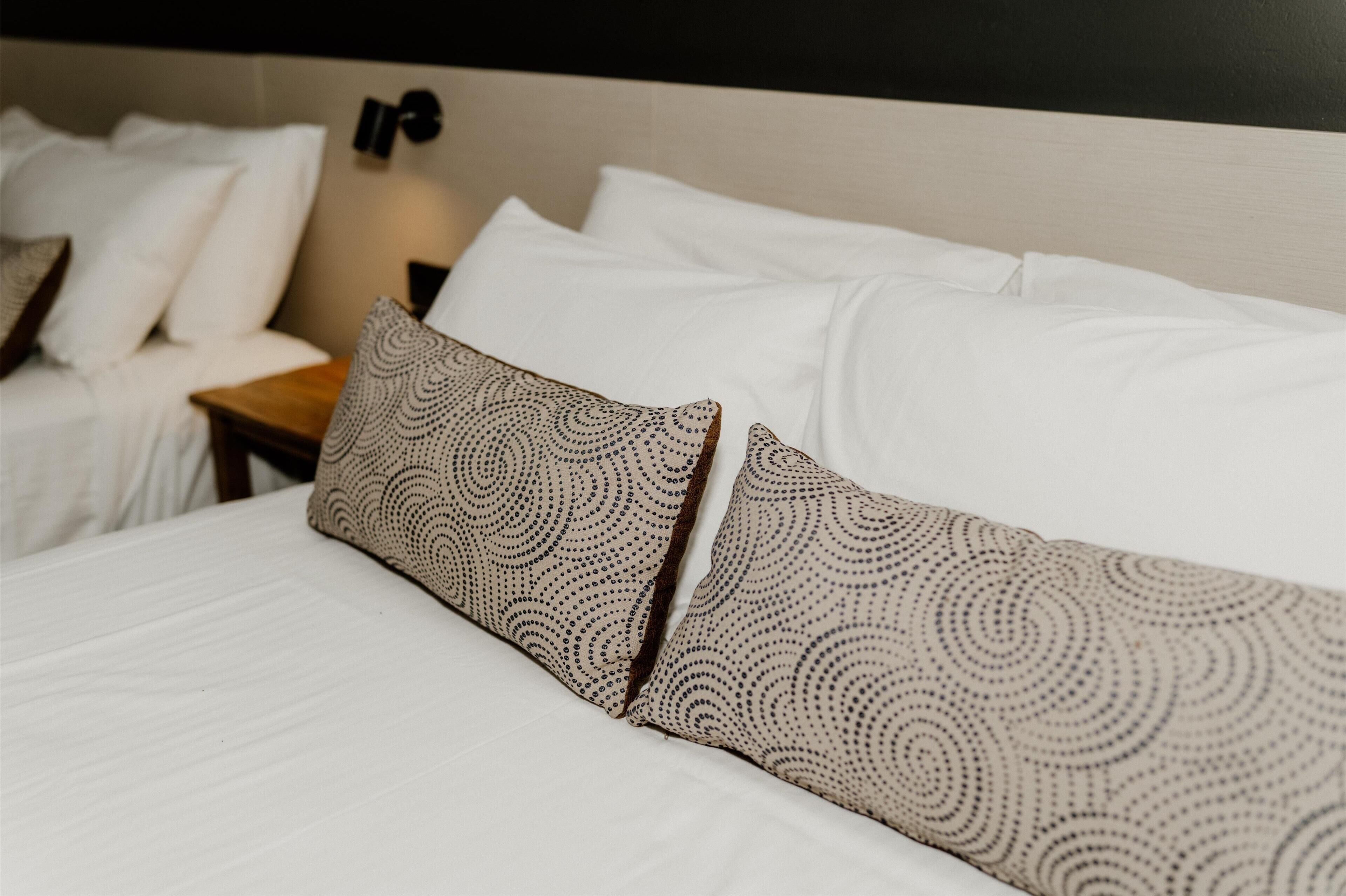 Cama bem arrumada com roupa de cama branca e almofadas estampadas.