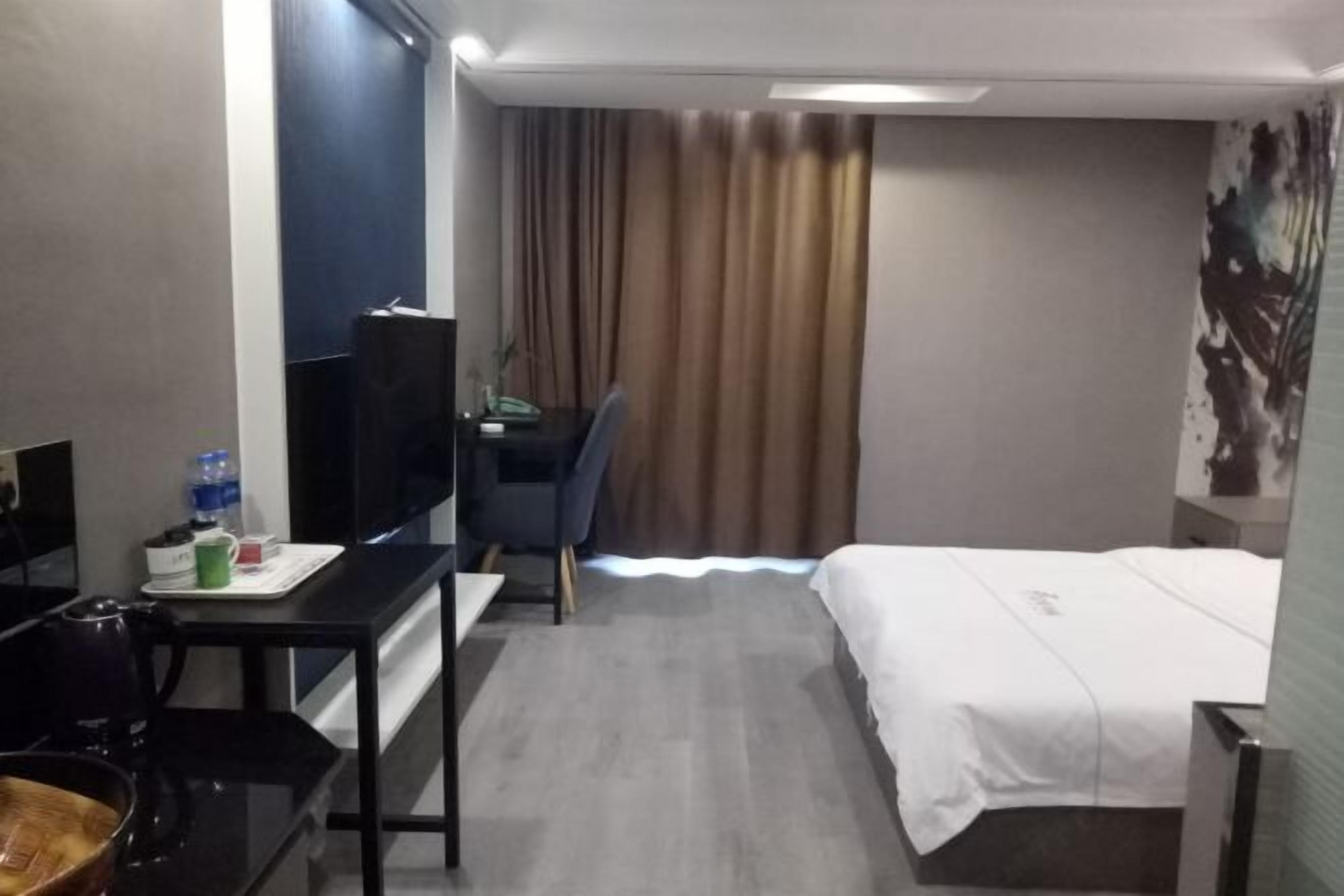 Quarto de hotel com uma cama, uma escrivaninha com cadeira, televisão e uma janela com cortinas.
