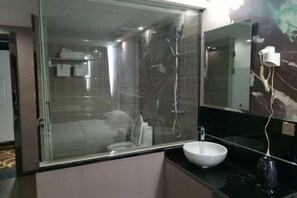 Casa de banho com cabine de chuveiro em vidro, lavatório branco e espelho com telefone.
