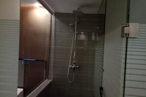 Pequeno espaço de chuveiro fechado, com chuveiro manual e torneira na parede.