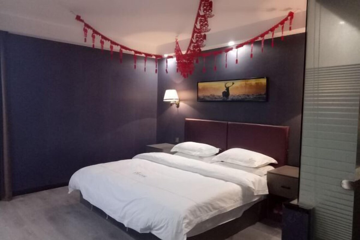 Quarto com cama, mesas de cabeceira, abajur fixado na parede e uma pintura.