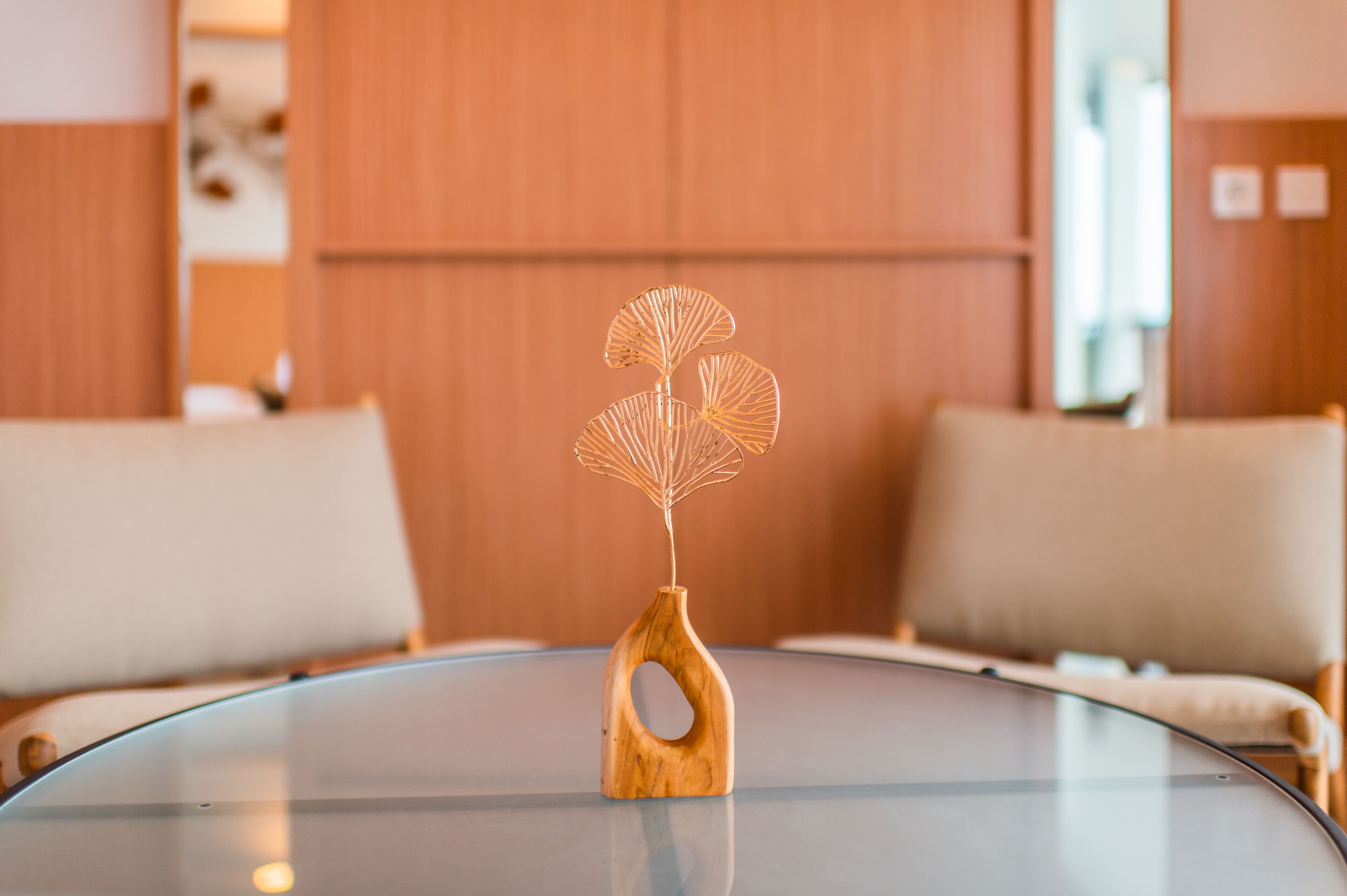 Uma mesa de vidro redonda com um vaso de madeira contendo uma escultura de folha de arame.