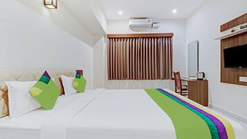 Quarto de hotel com cama, cortinas, ar condicionado, televisão e escrivaninha com cadeira.