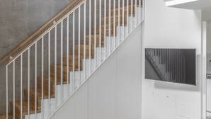 Interior moderno com escada de madeira, paredes brancas e televisão de tela plana fixada na parede.