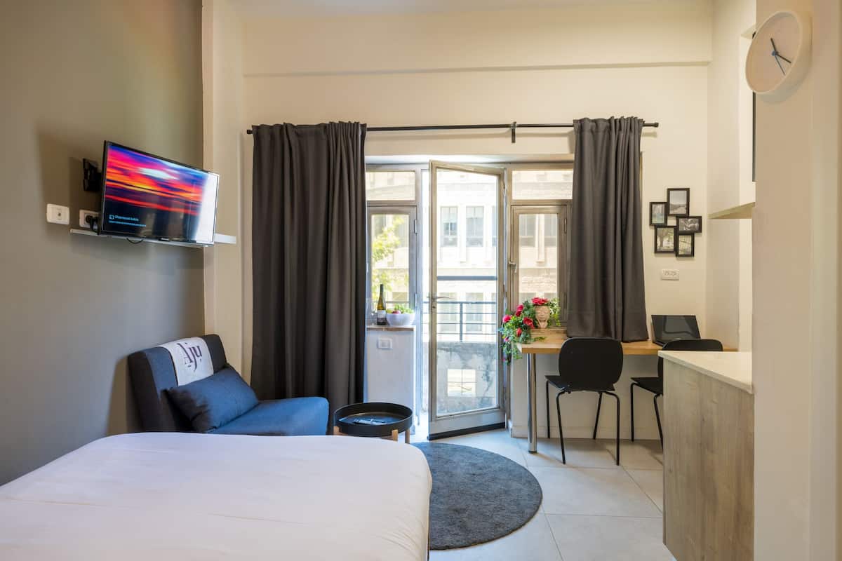 Quarto de hotel com cama, escrivaninha, cadeira, televisão e varanda com cortinas.