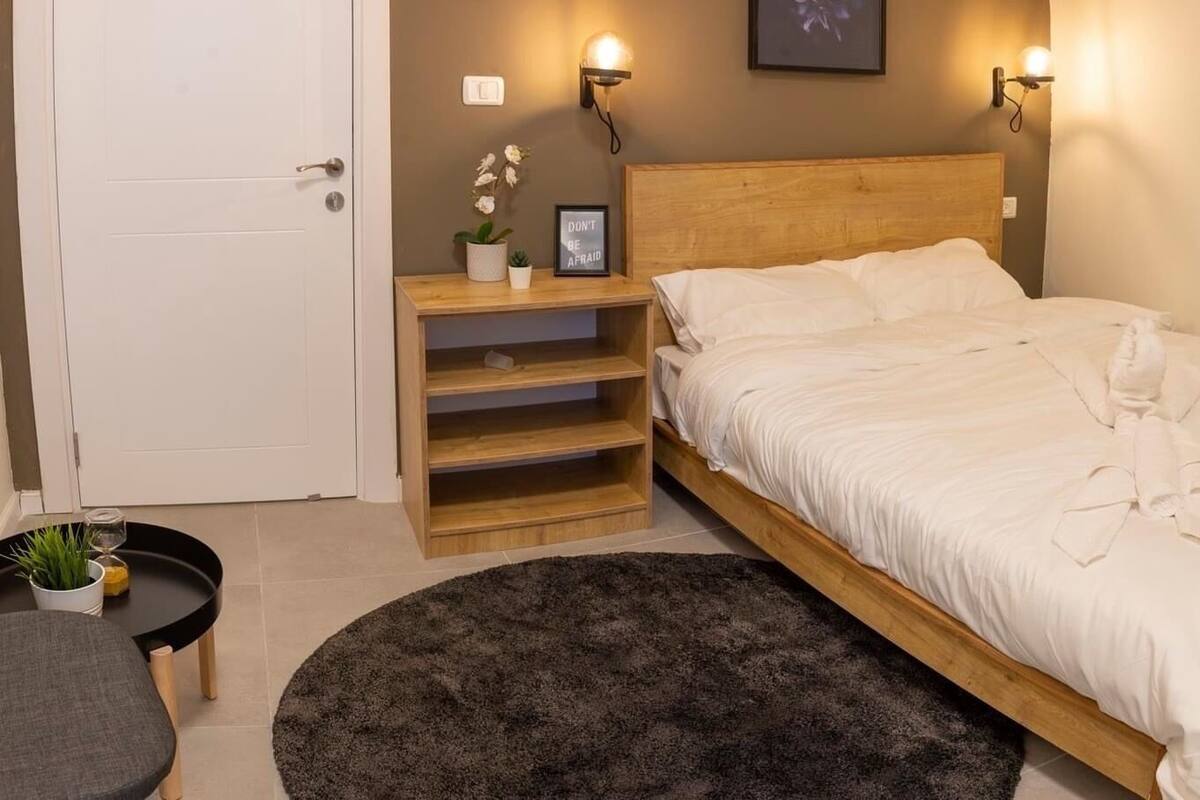 Quarto com cama, mesa de cabeceira, cadeira e uma pequena mesa com uma planta.