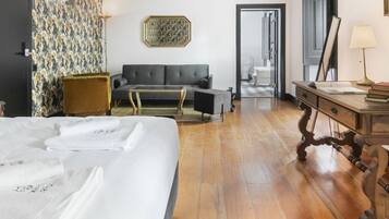 Quarto de hotel com uma cama grande, um sofá, uma escrivaninha de madeira e vista para o corredor.