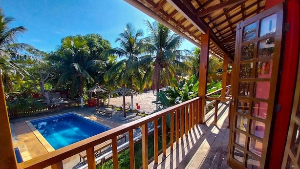 Um deck de madeira com piscina, cercado por palmeiras e um céu claro.