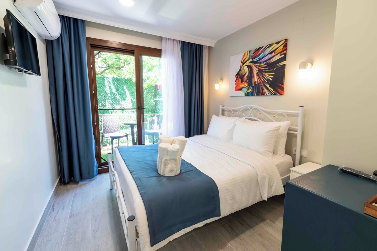 Quarto de hotel com cama, uma mesa pequena, uma cadeira, televisão e um quadro na parede.
