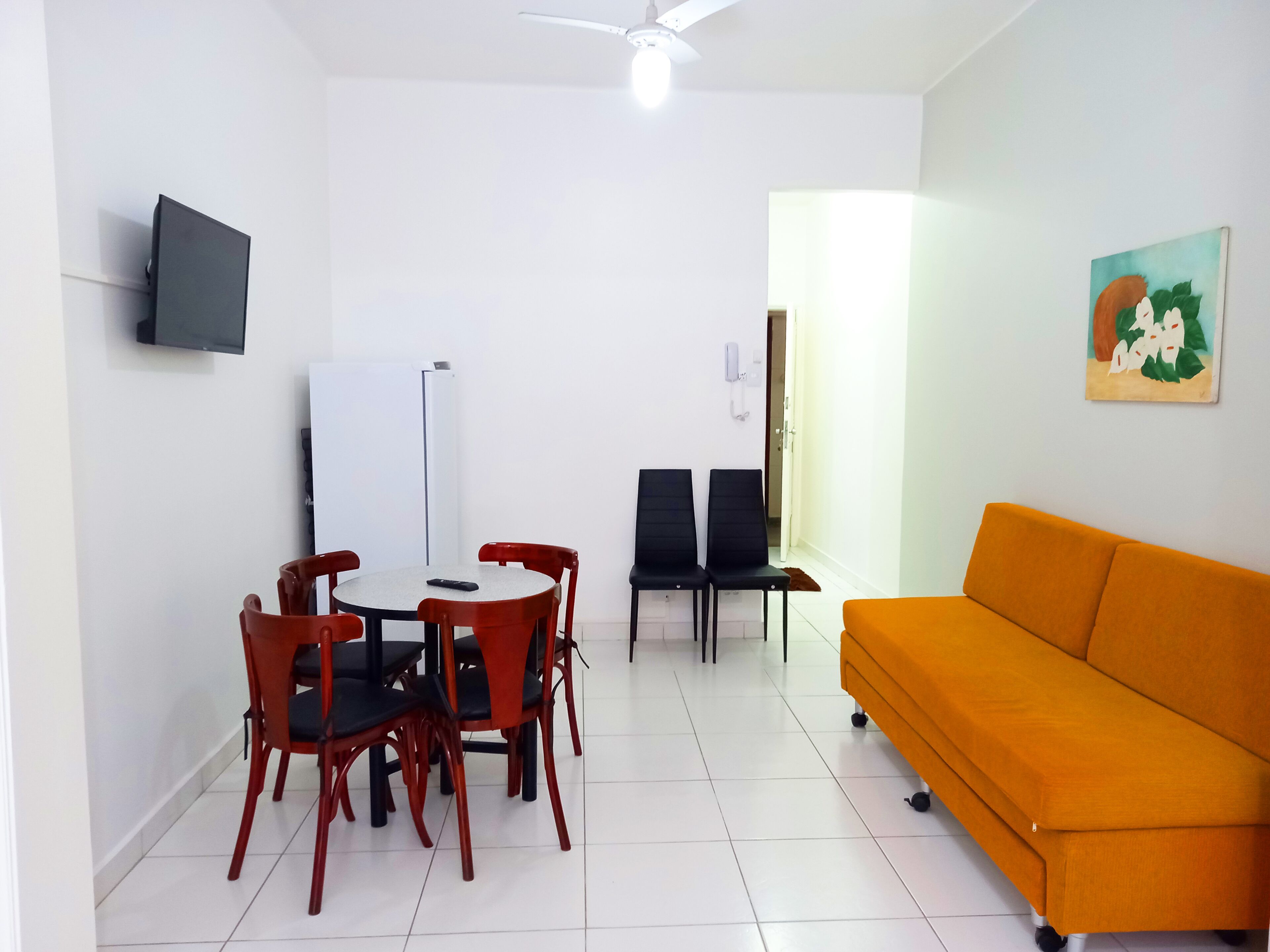 Um quarto com uma mesa de jantar, cadeiras, um sofá, uma televisão e um quadro na parede.