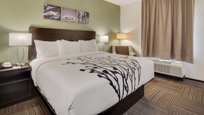Quarto de hotel com uma cama grande, duas mesas de cabeceira, um criado-mudo, uma lâmpada fixada na parede, uma janela com cortinas e um radiador.