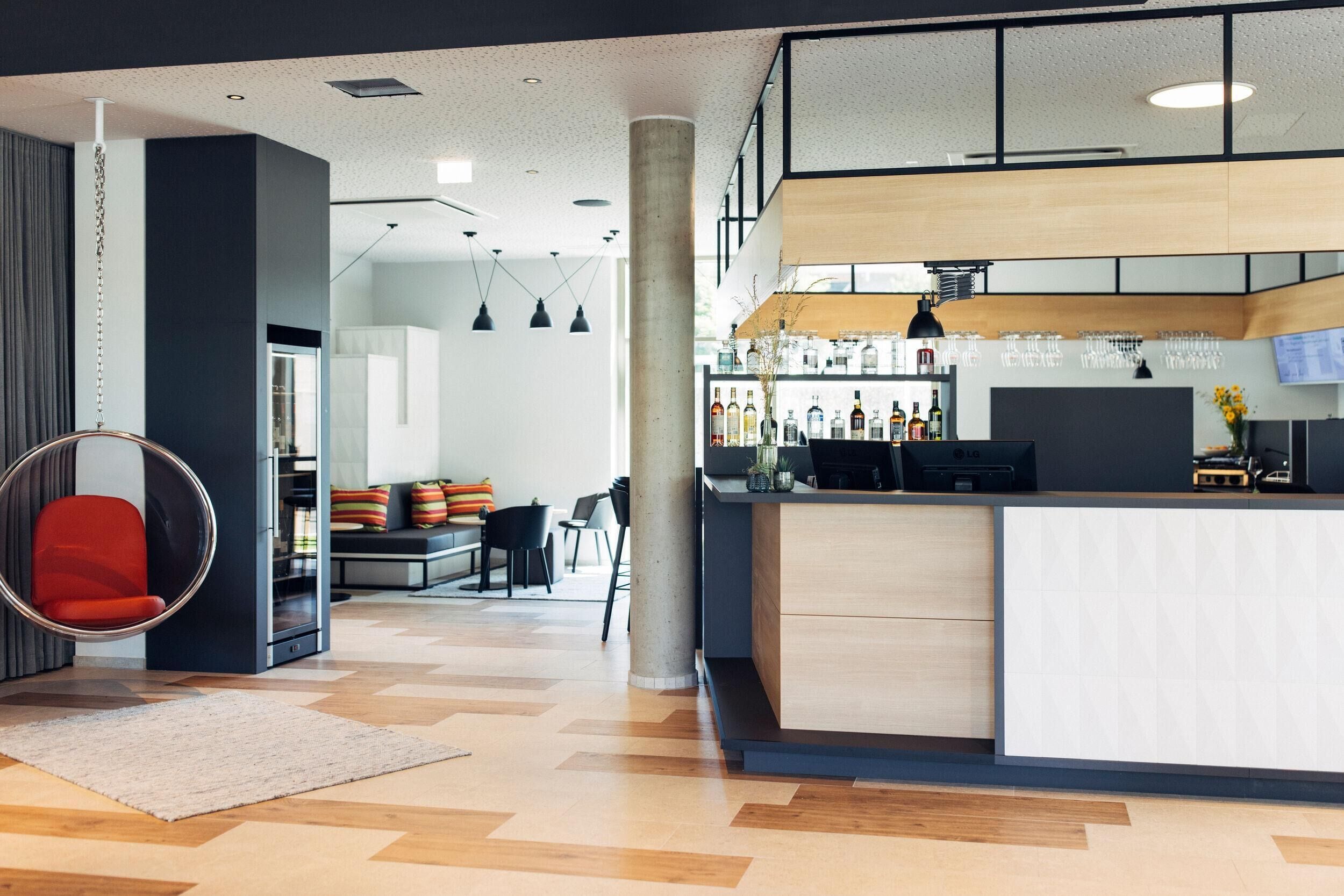 Um lobby de hotel moderno com área de bar, assentos e uma cadeira suspensa.