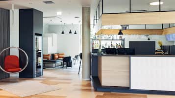 Um lobby de hotel moderno com área de bar, assentos e uma cadeira suspensa.