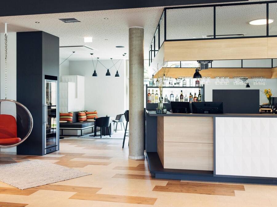 Um lobby de hotel moderno com área de bar, assentos e uma cadeira suspensa.