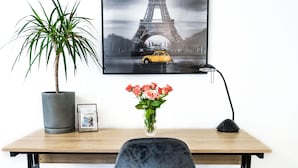 Uma mesa com uma cadeira, um vaso de plantas, um vaso com flores, um quadro emoldurado e um abajur.