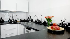 Cozinha com armários brancos, bancada preta e painel decorativo com vista urbana.